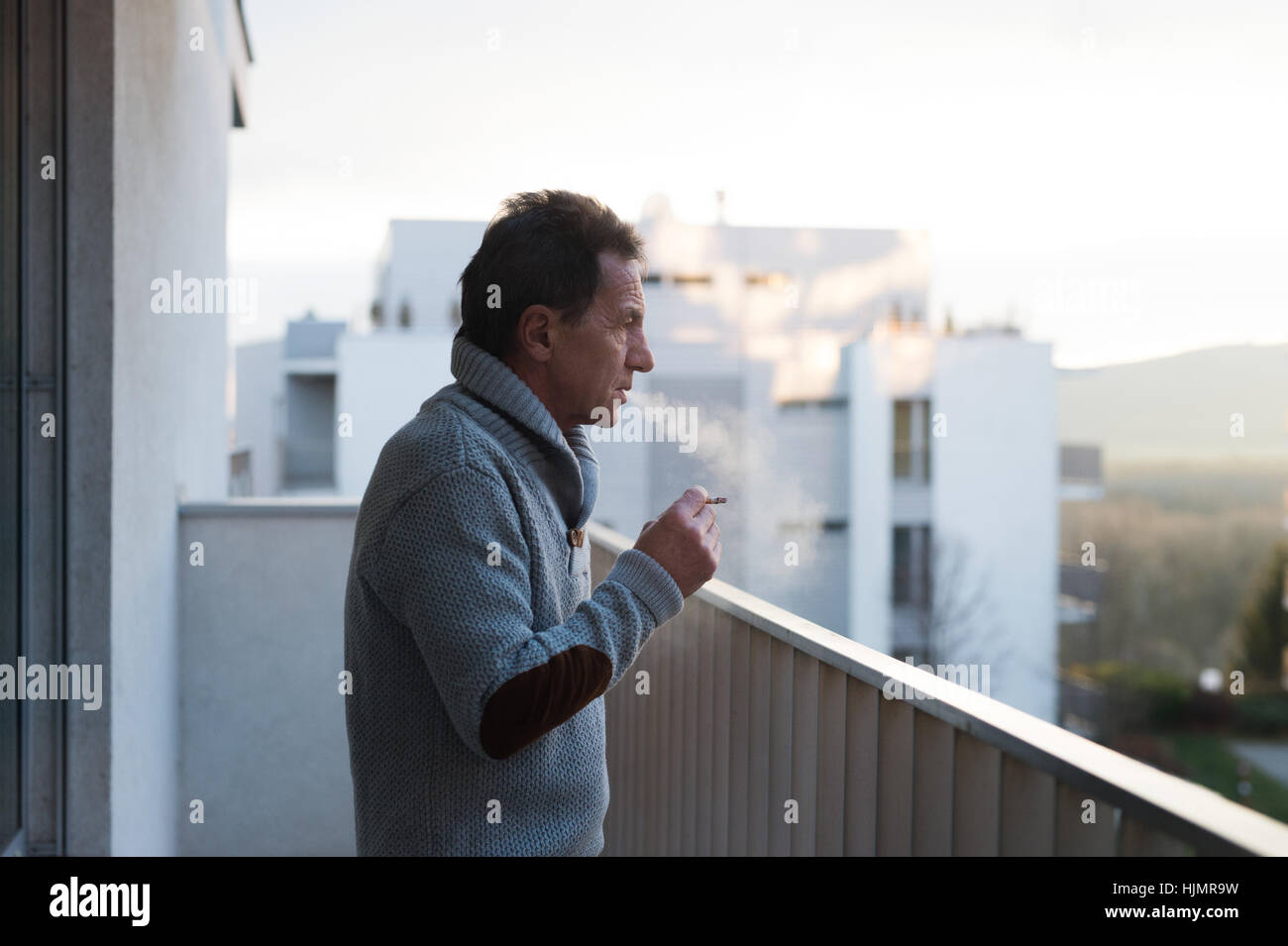 Serious senior man standing on balcony, smoking a cigarette Stock Photo ...
