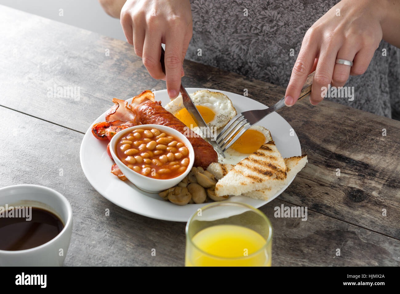 Woman eating a traditional English breakfast with fried eggs, sausages ...