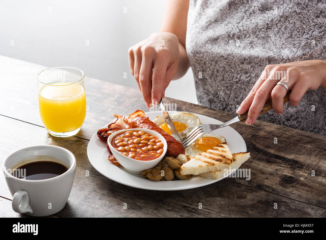 Woman eating a traditional English breakfast with fried eggs, sausages ...