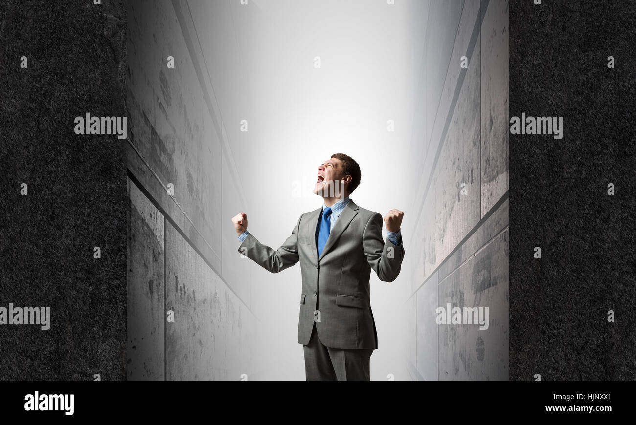 Young confident businessman with hands up screaming emotionally above ...
