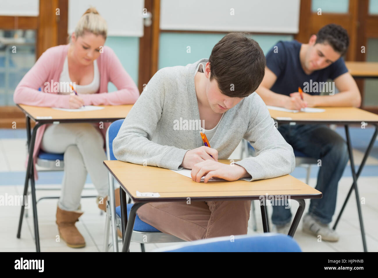 Three students sitting in a classroom at a desk and writing Stock Photo ...