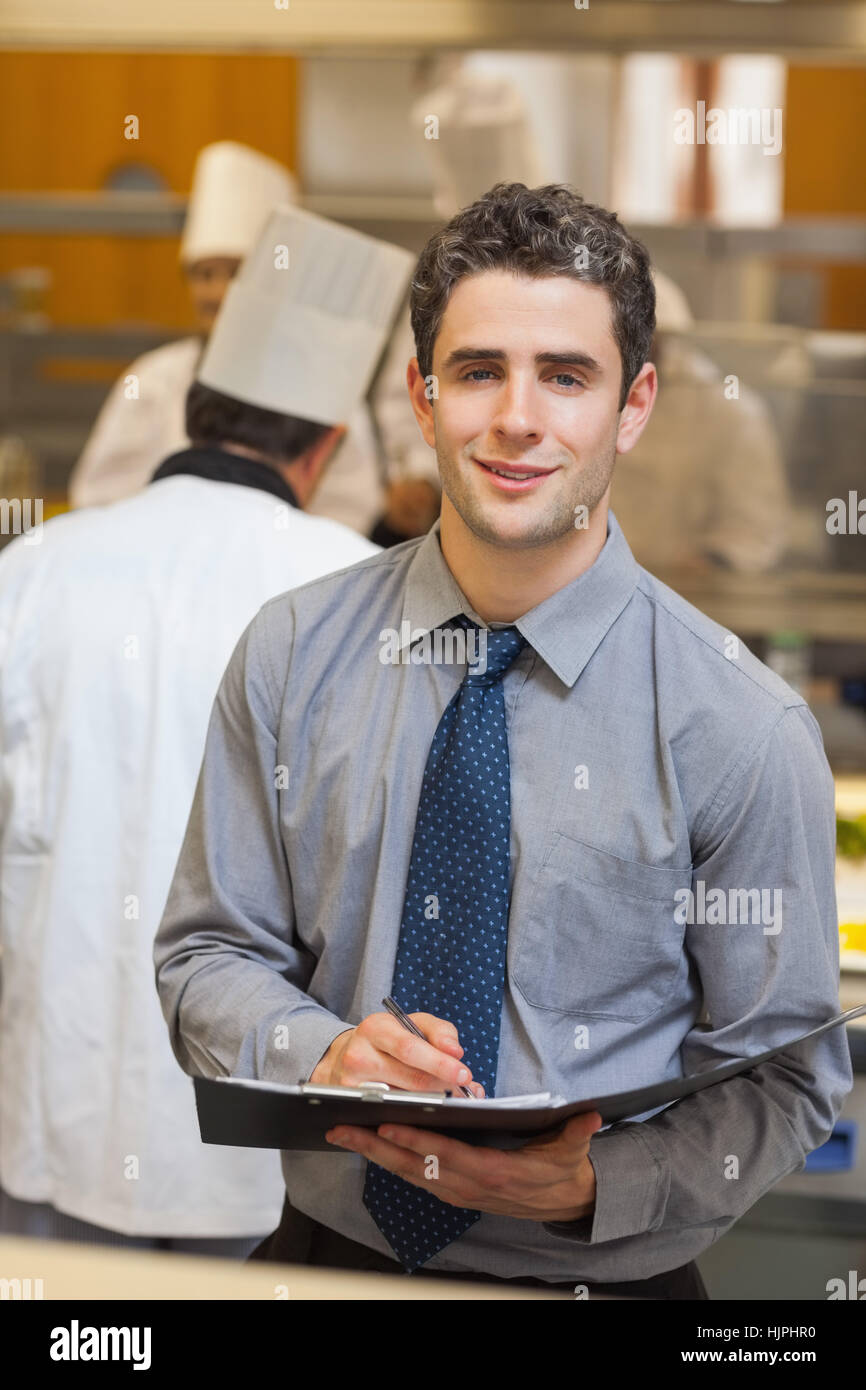 Smiling waiter writing in folder in kitchen Stock Photo - Alamy