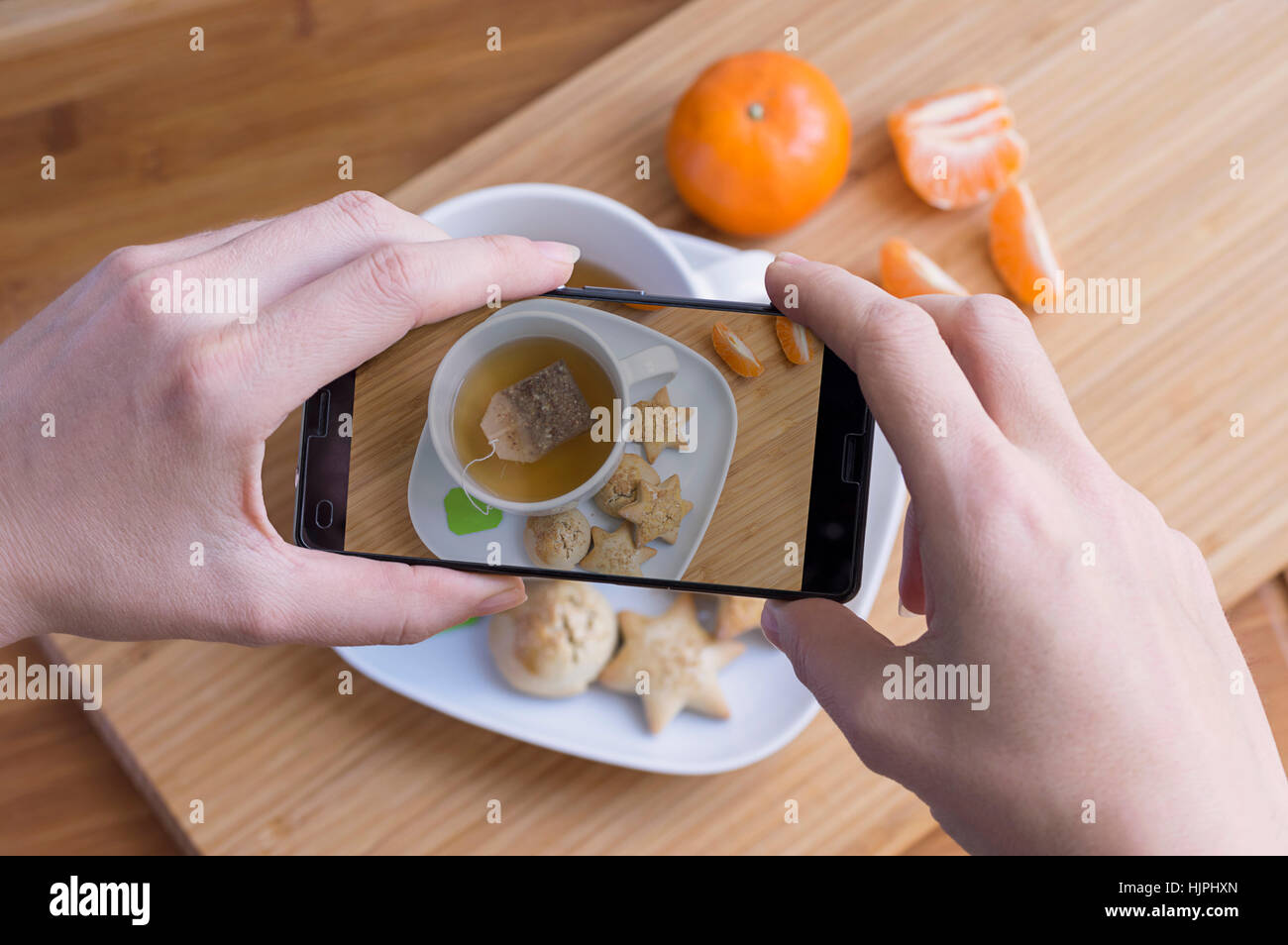 Woman taking photo of tea breakfast and tangerine with mobile phone ...