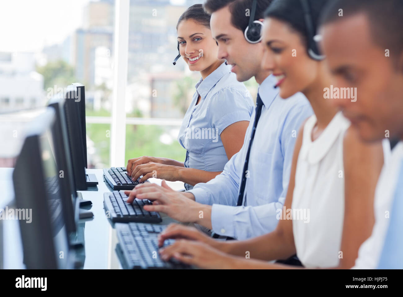 Smiling call centre employees working on computers with their headsets ...