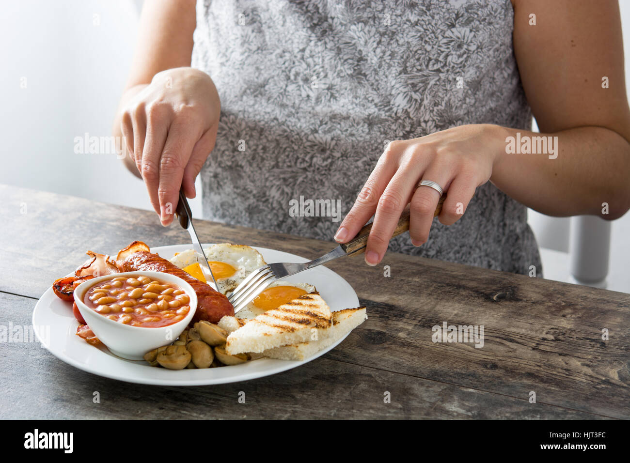 Woman eating a traditional English breakfast with fried eggs, sausages ...