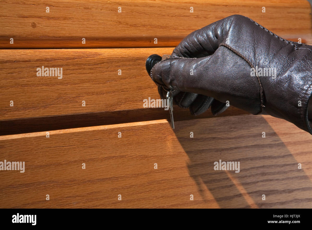 Leather gloved hand turning key in lock of wooden desk Stock Photo - Alamy