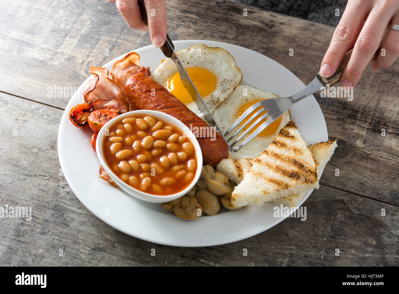 Woman eating a traditional English breakfast with fried eggs, sausages ...