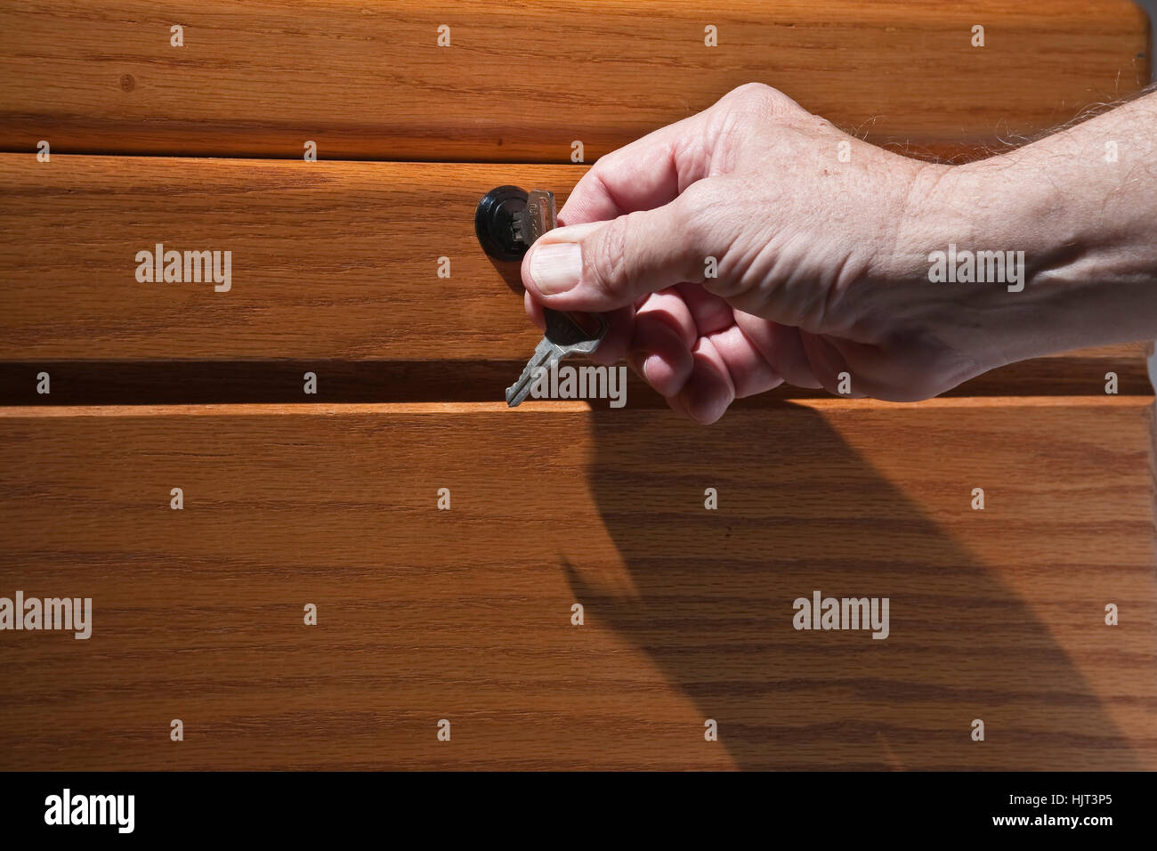 Older man's hand turning key in lock of wooden desk Stock Photo - Alamy
