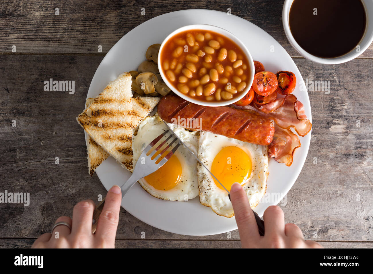Woman eating a traditional English breakfast with fried eggs, sausages ...
