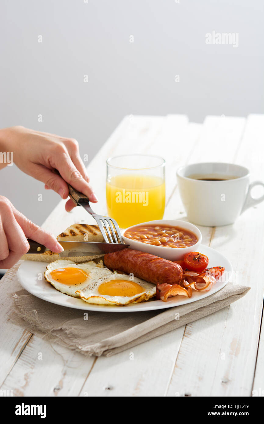 Woman eating a traditional English breakfast with fried eggs, sausages ...