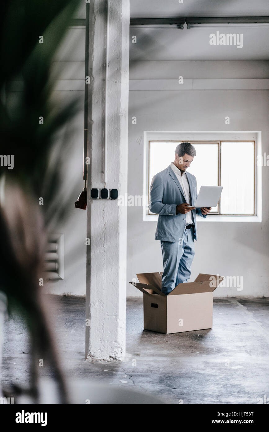 Businessman using laptop inside cardboard box in empty loft Stock Photo ...