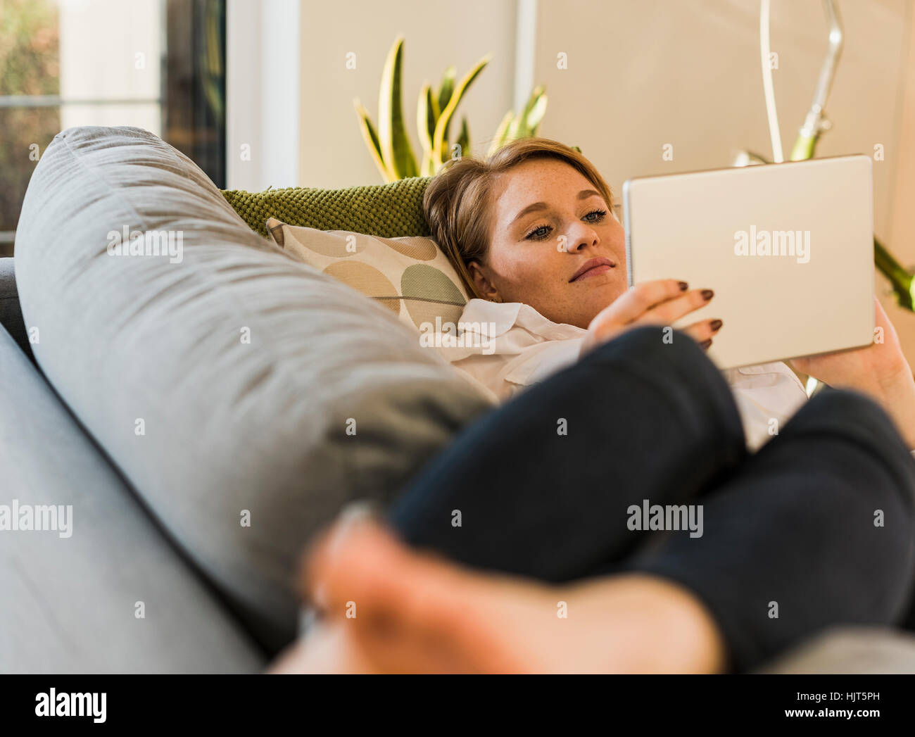 Young woman lying on couch using tablet Stock Photo - Alamy