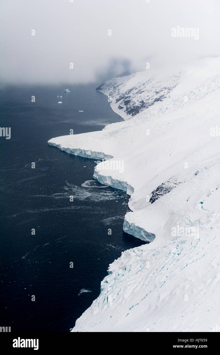 Cliffs covered in snow and ice tower above a dark ocean surface Stock ...