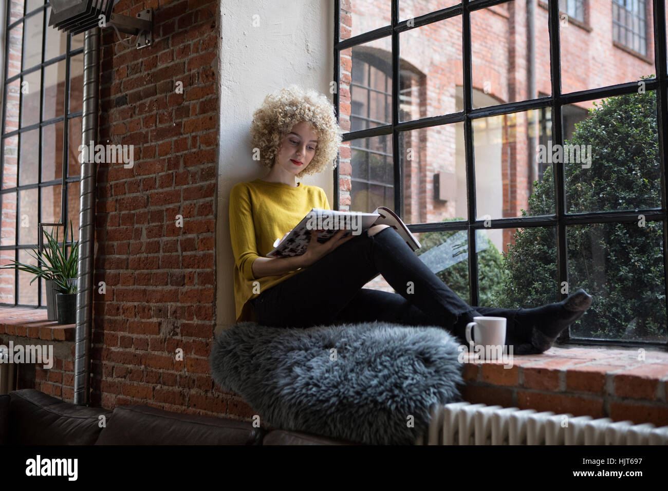 Young woman sitting on window sill Stock Photo - Alamy