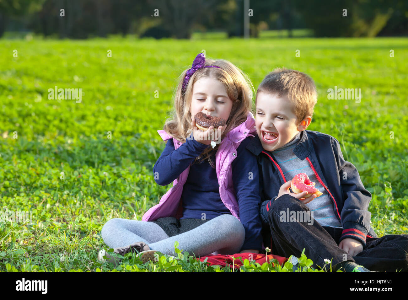 happy kids eating donuts sitting on the green grass in the park Stock ...