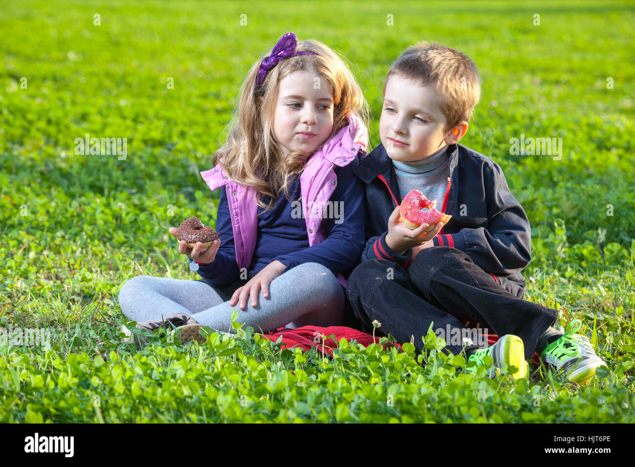 happy kids eating donuts sitting on the green grass in the park Stock ...