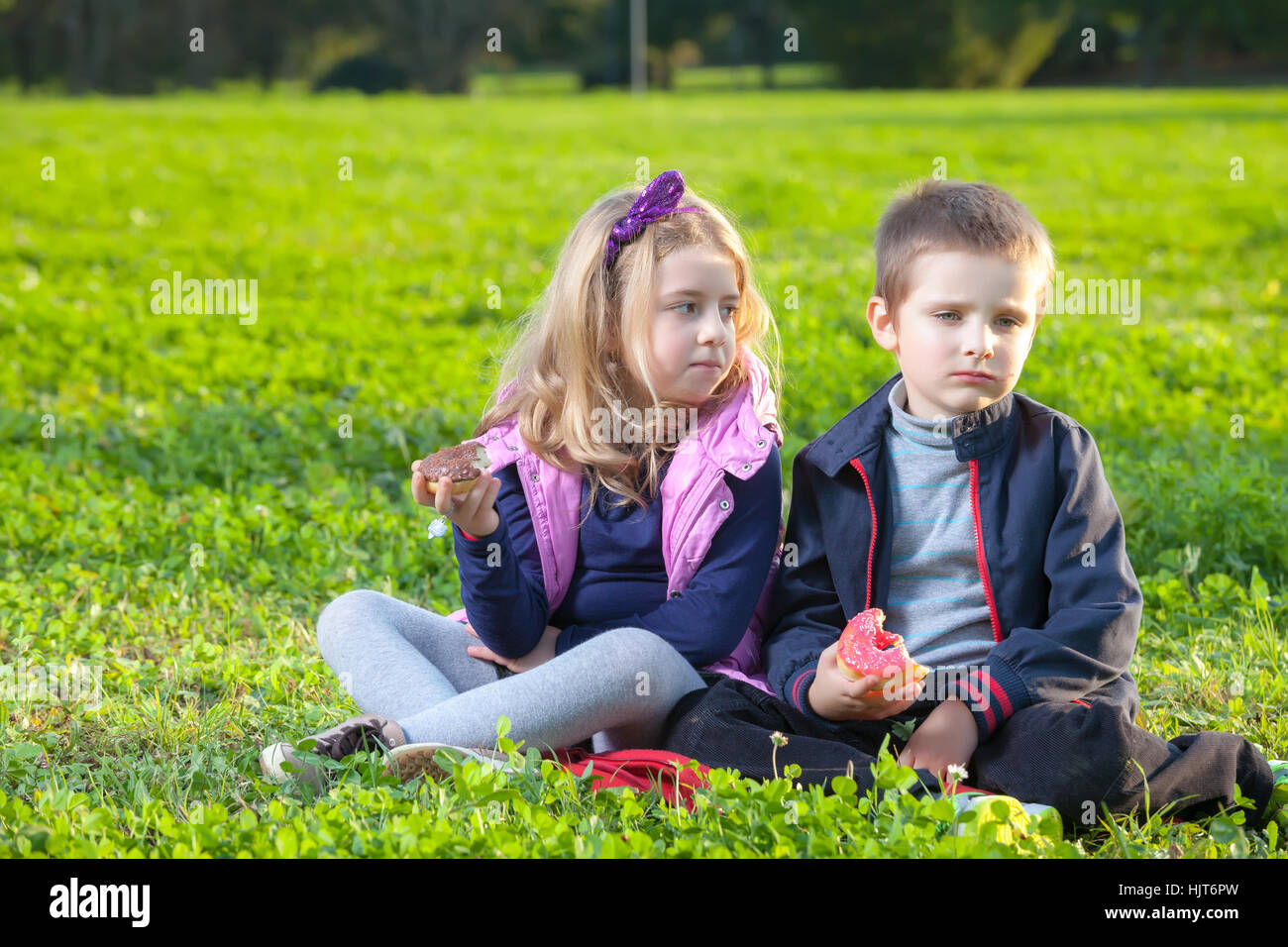 happy kids eating donuts sitting on the green grass in the park Stock ...
