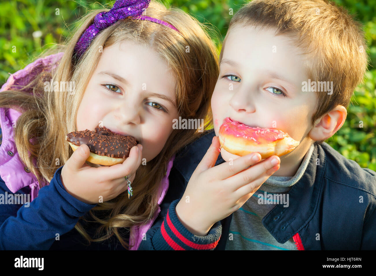 happy kids eating donuts sitting on the green grass in the park Stock ...
