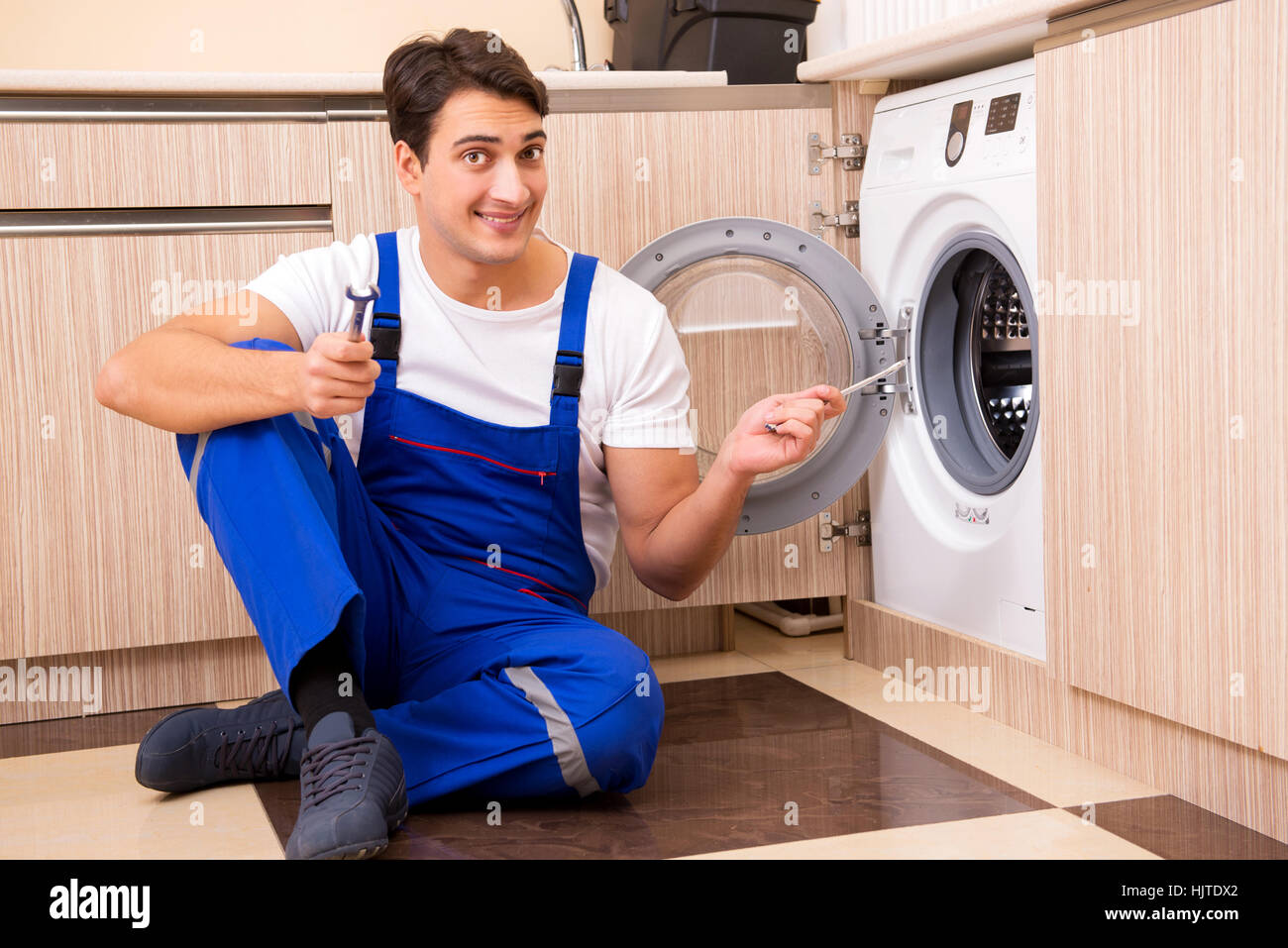 Repairman repairing washing machine at kitchen Stock Photo - Alamy