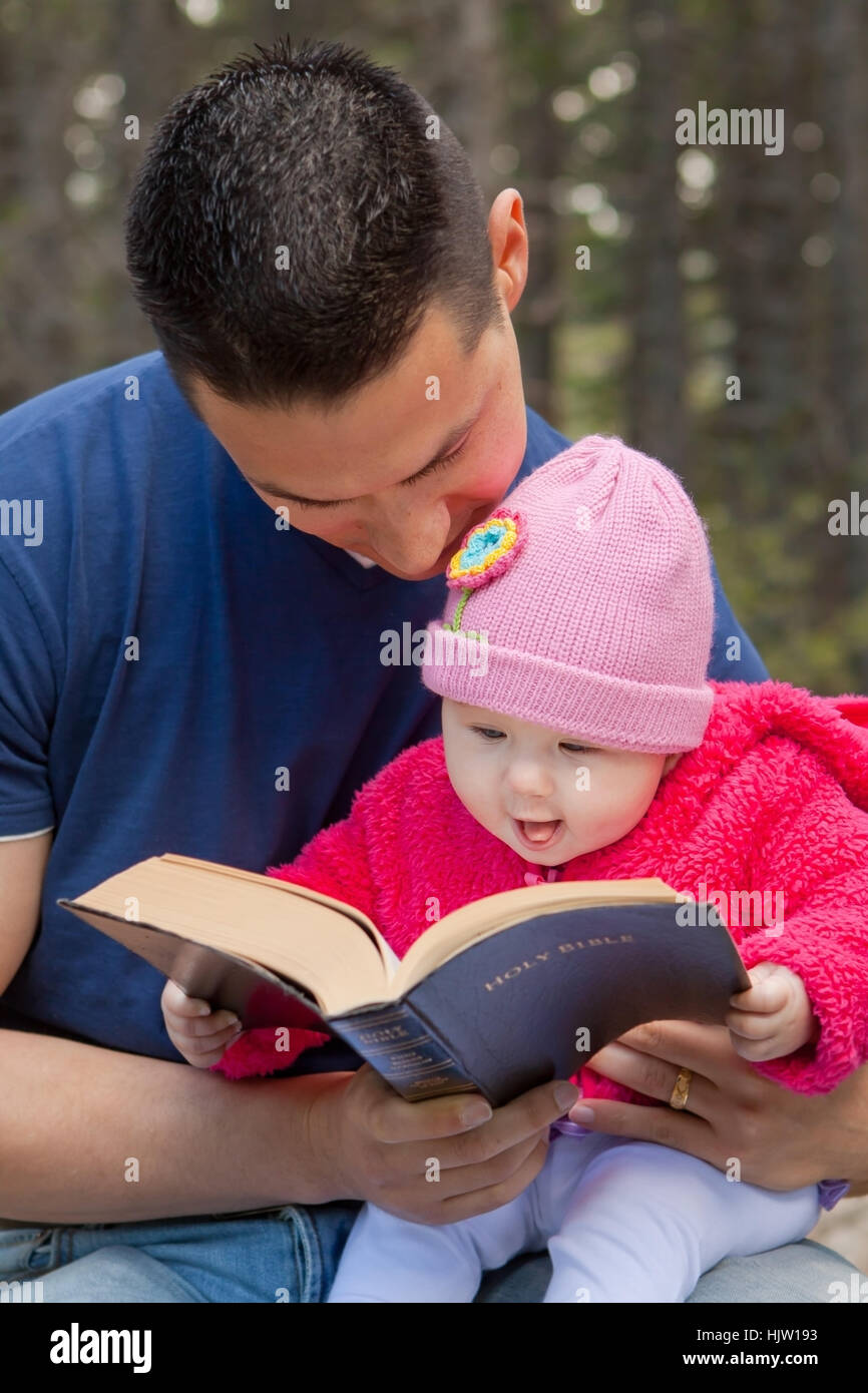 Baby girl sitting on dad’s lap reading KJV Bible (King James Version ...