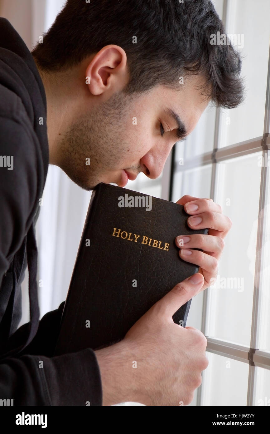 Young man holding Bible and praying by window Stock Photo - Alamy