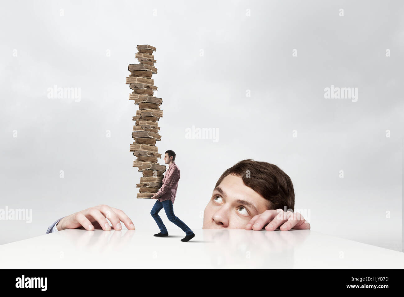 Young businessman looking from under table at man carrying pile of ...
