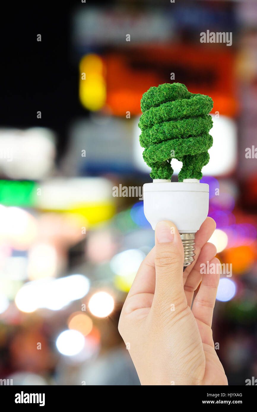 hand holding green light bulb and defocused city night light background ...