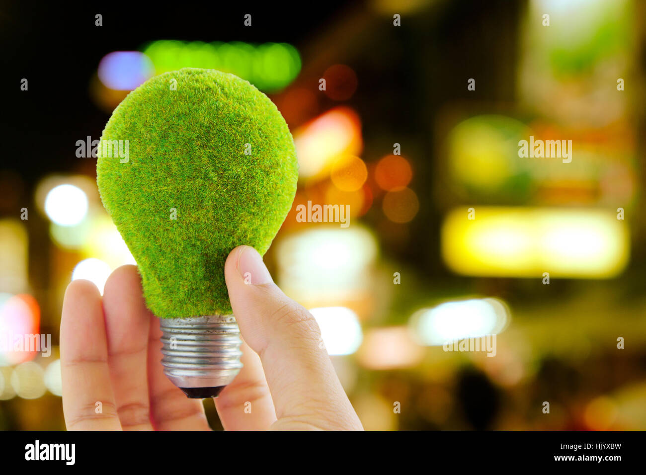 hand holding green light bulb and defocused city night light background ...
