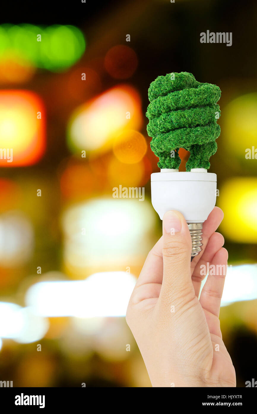 hand holding green light bulb and defocused city night light background ...