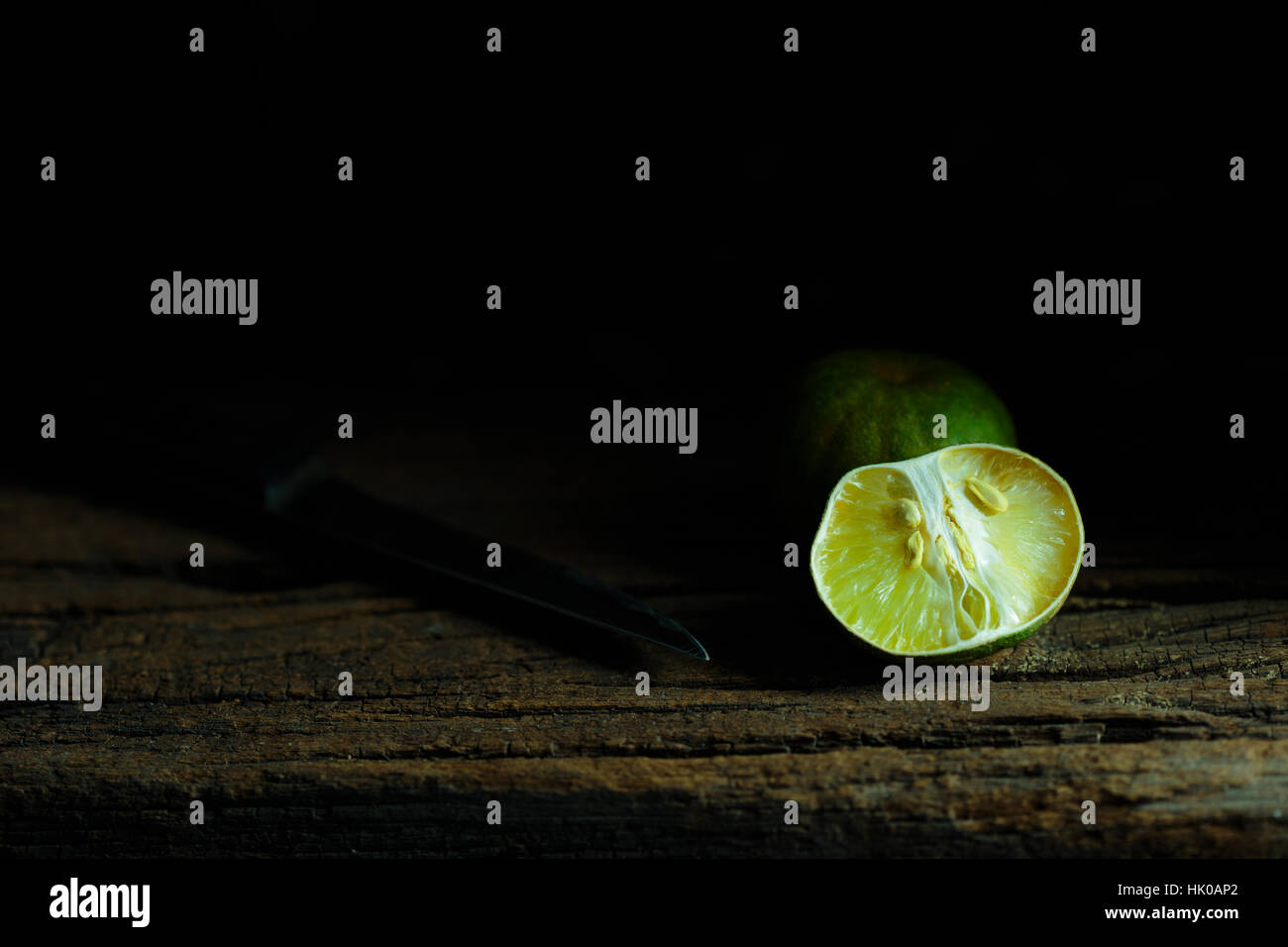 Lemon and side of lemon and knife on wood plate with moody and dark ...