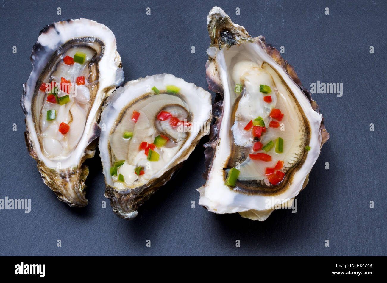 Three oysters prepared with red and green chilli served on a slate ...