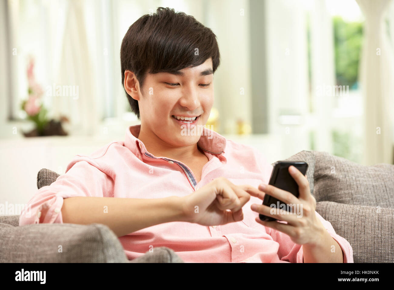 Young Chinese Man Using Mobile Phone On Sofa At Home Stock Photo - Alamy