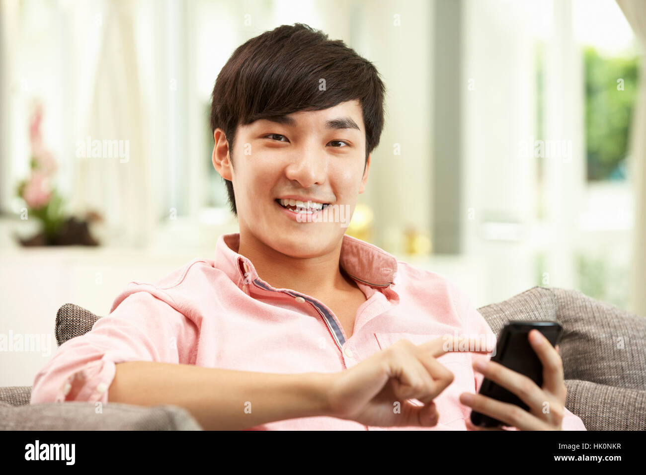 Young Chinese Man Using Mobile Phone On Sofa At Home Stock Photo - Alamy