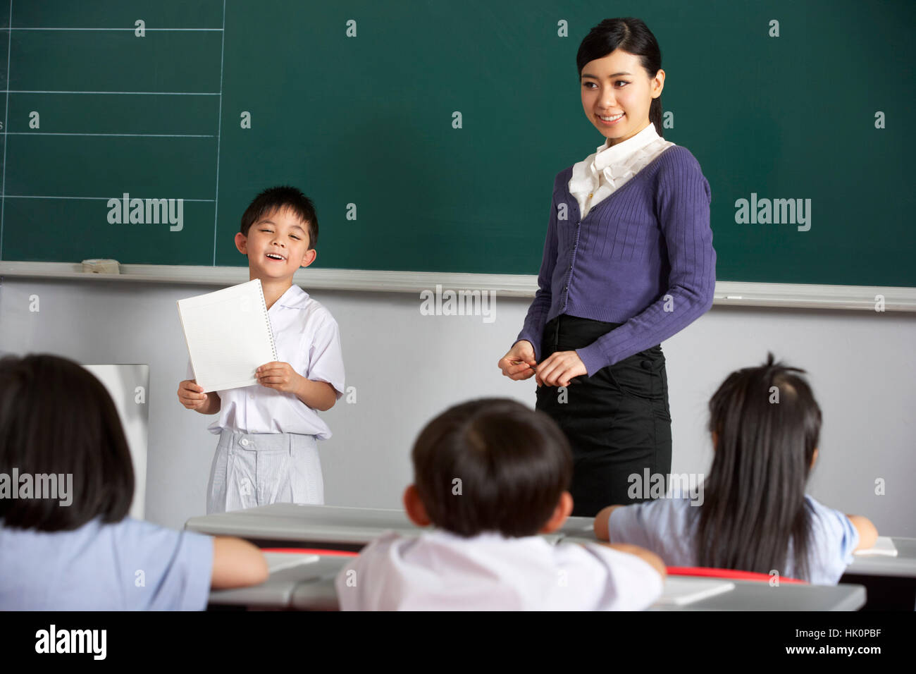 Pupil And Teacher Standing By Blackboard In Chinese School Classroom ...