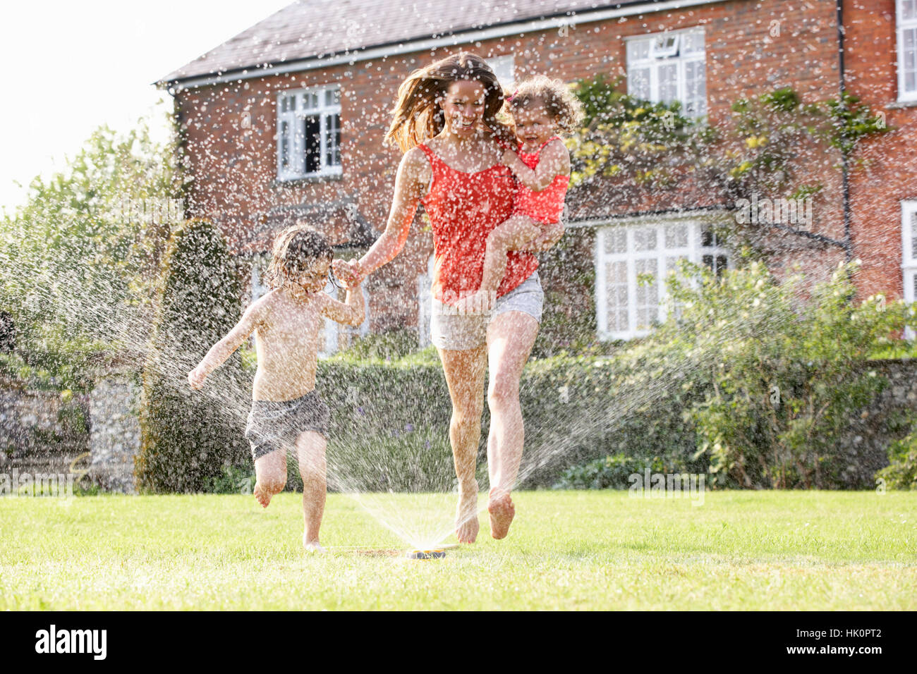 Mother And Two Children Running Through Garden Sprinkler Stock Photo ...