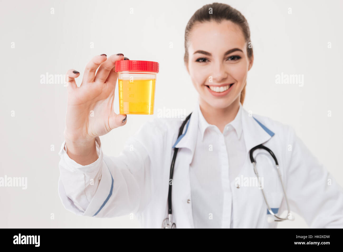 Cheerful young woman doctor standing and holding bottle of urine sample ...