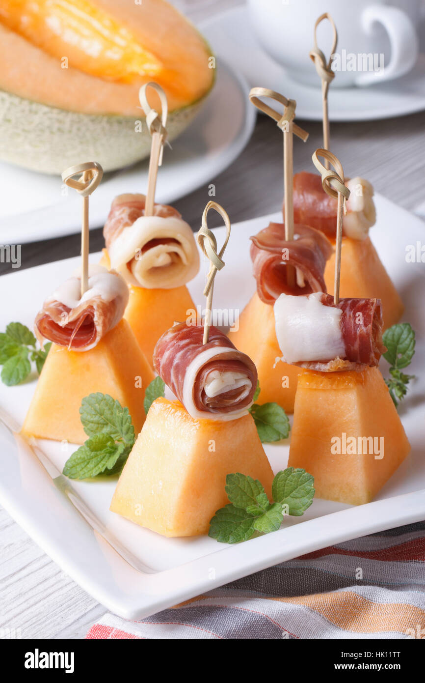 Italian appetizer: melon with ham on skewers on a plate close up ...