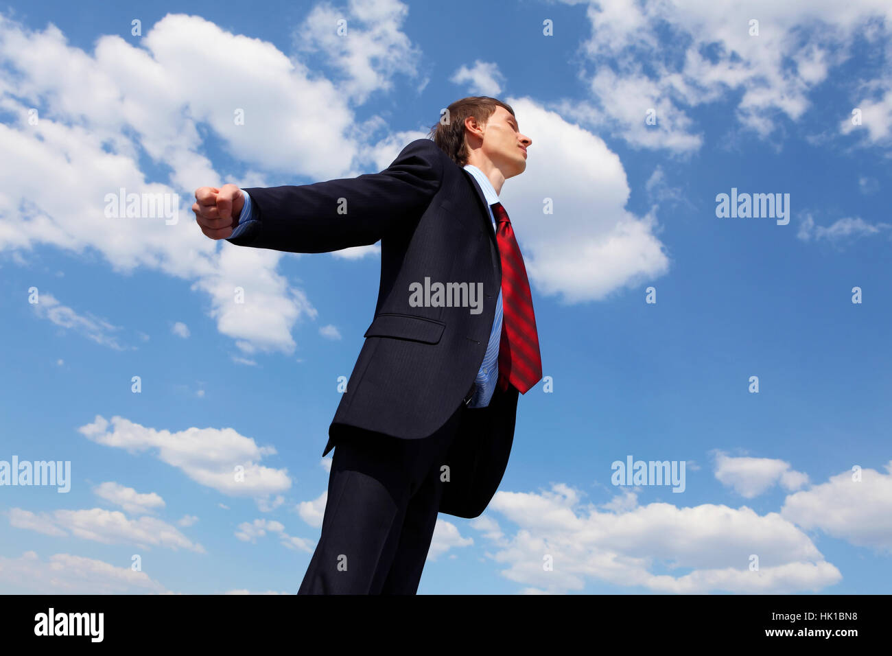 Young businessmanin a blue suit embracing air against blue sky hi-res ...