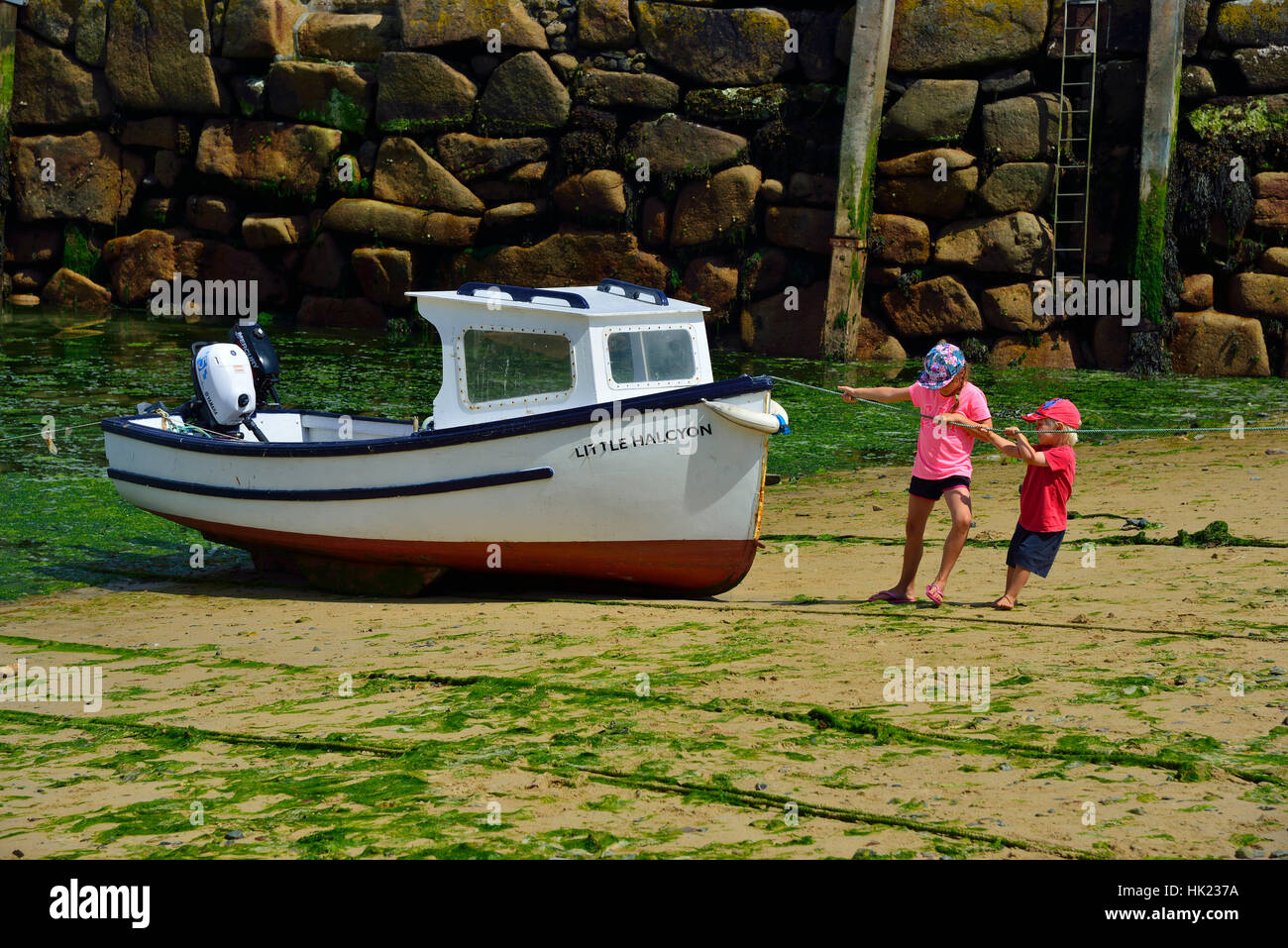 Two small children playing on the seashore and pulling on a rope from a ...