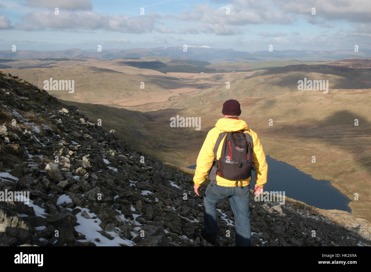 Rear view of hill walker traversing steep scree slope on bright sunny ...