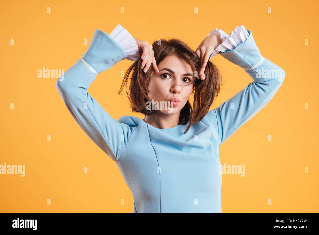 Playful comical young woman joking and making funny face over yellow ...