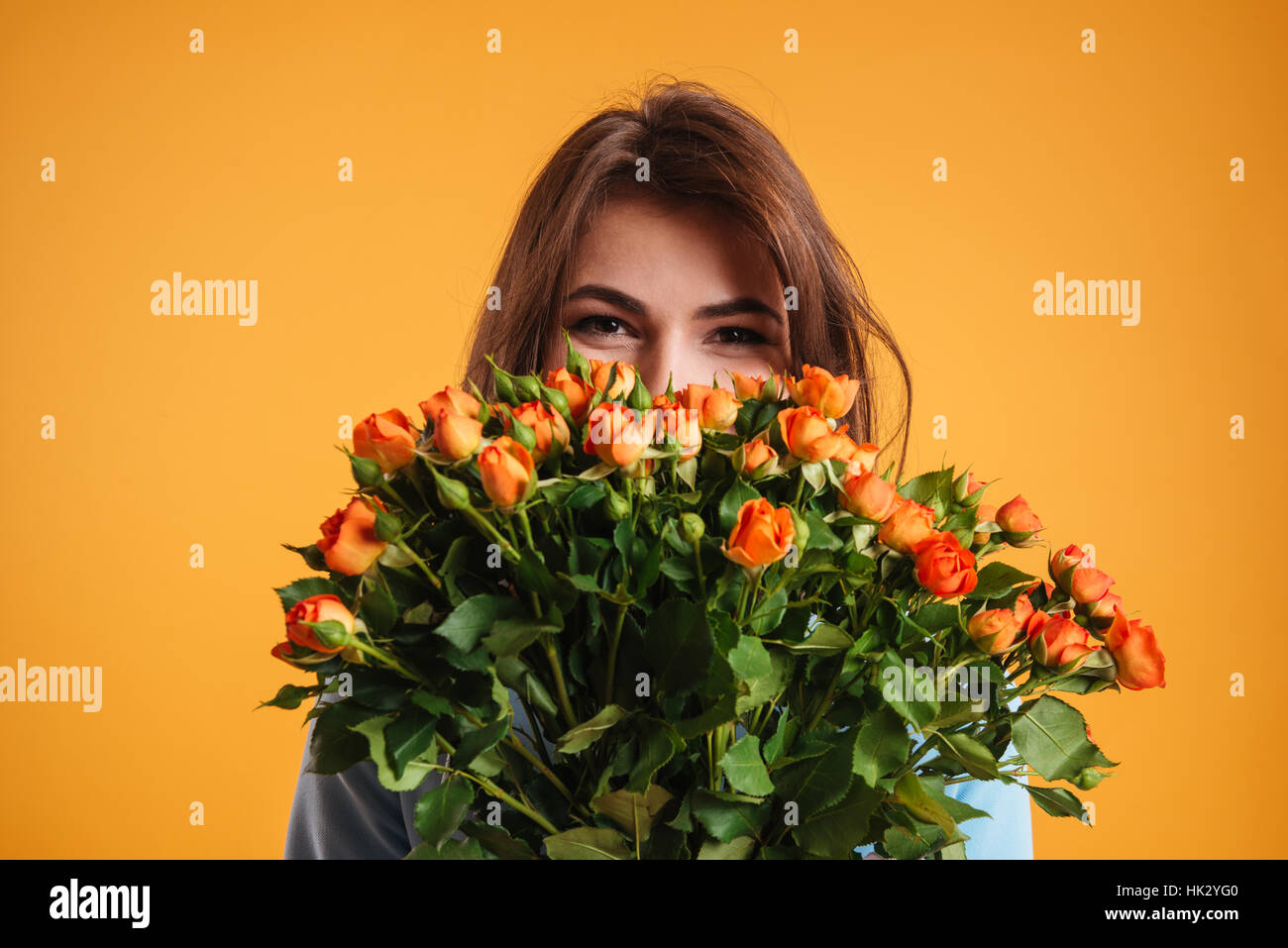 Smiling cute young woman standing and hiding behind bouquet of flowers ...