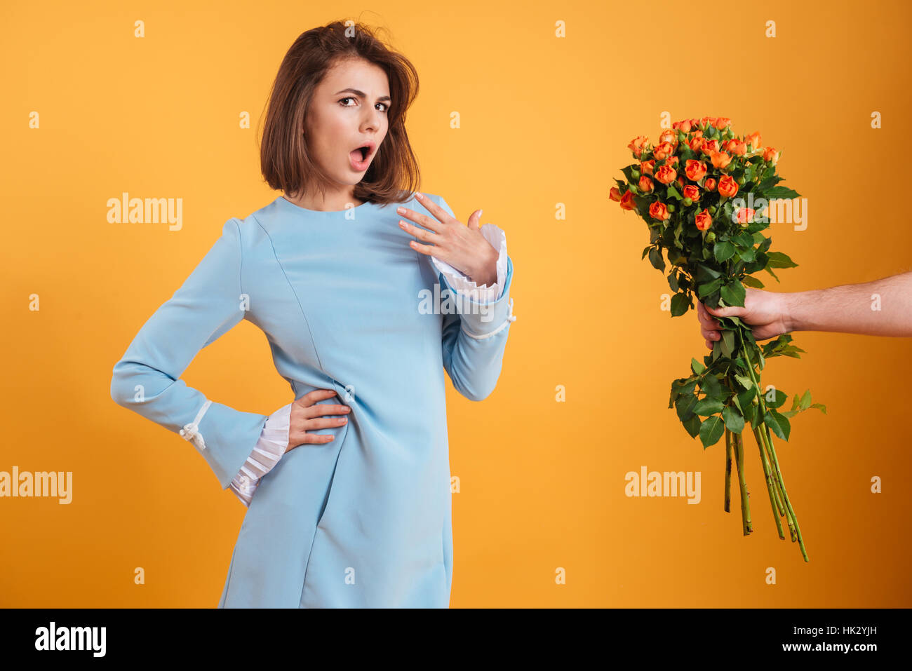 Surprised pretty young woman receiving bouquet of flowers over yellow ...