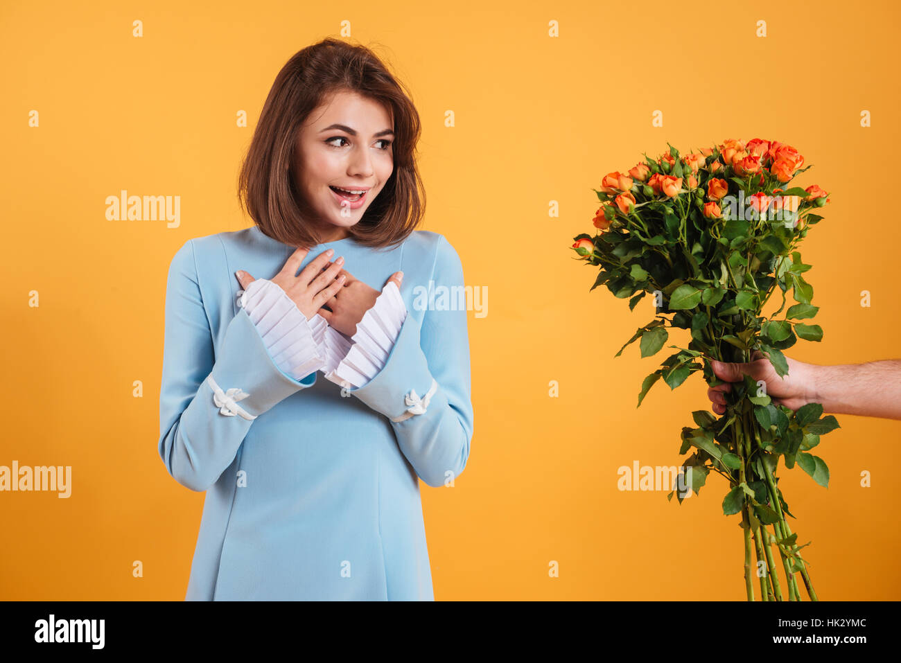 Smiling surprised young woman standing and receiving bouquet of flowers ...