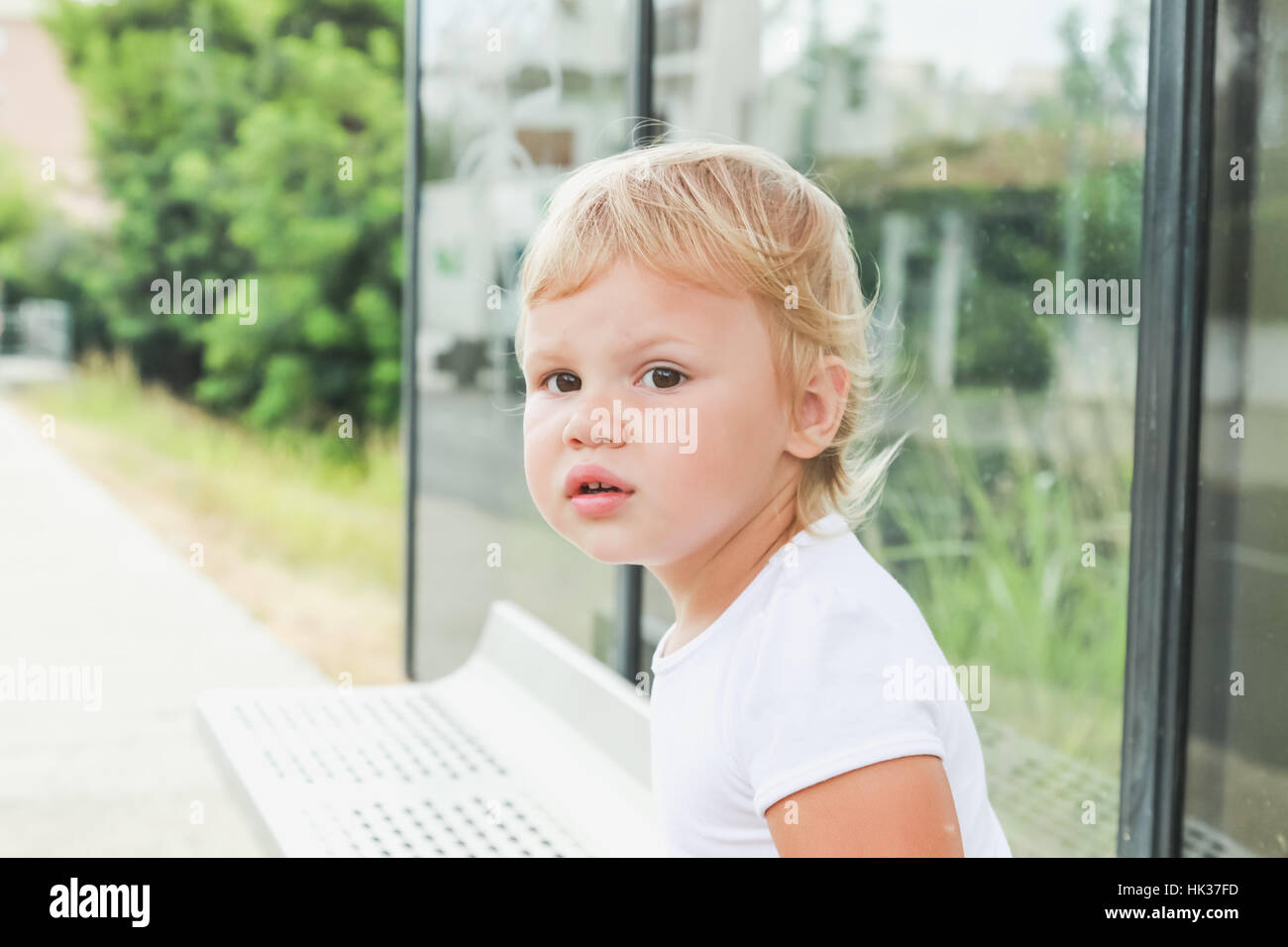 Close-up portrait. Cute Caucasian blond baby girl waits on a bus stop ...