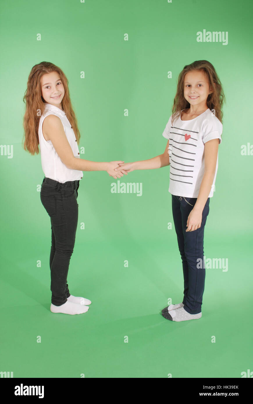 Young school girls holding hands and smiling at camera. Studio shot on ...
