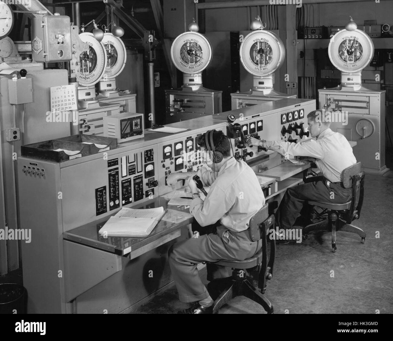 Two men sit at a console with dials and gauges and operate equipment ...