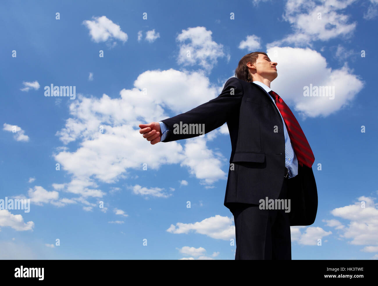 Young businessmanin a blue suit embracing air against blue sky hi-res ...