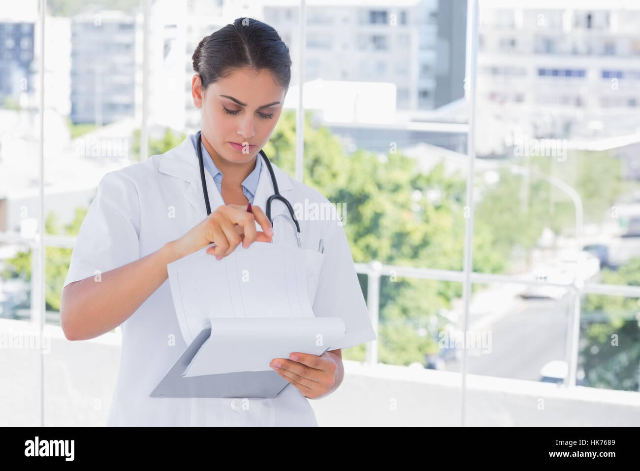 Doctor going through notes on clipboard attentively by large windows ...