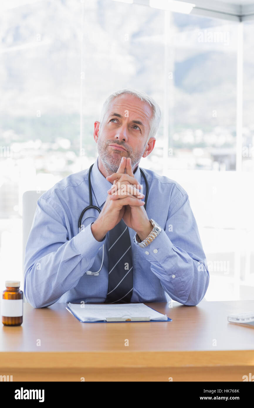 Doubtful doctor sitting behind his desk Stock Photo - Alamy